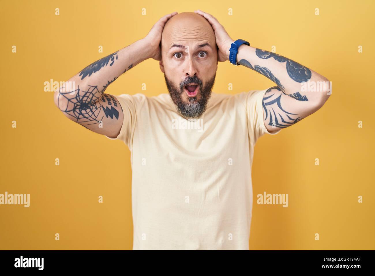Hispanic man with tattoos standing over yellow background crazy and ...