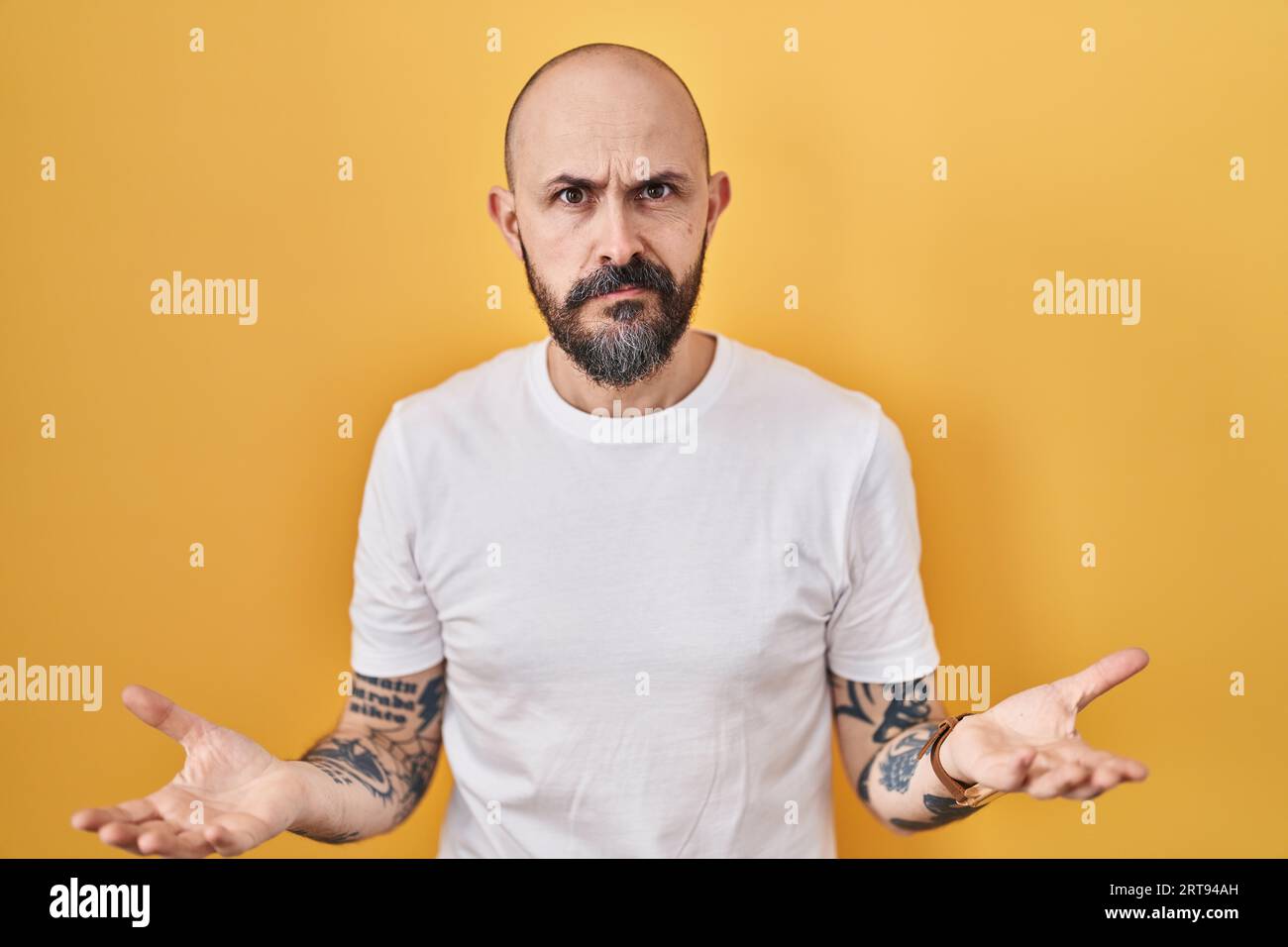 Young hispanic man with tattoos standing over yellow background ...