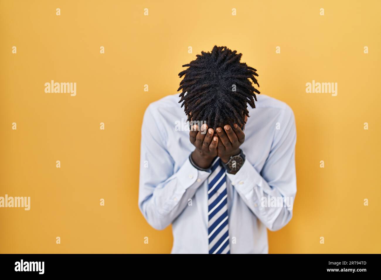 African man with dreadlocks standing over yellow background with sad ...