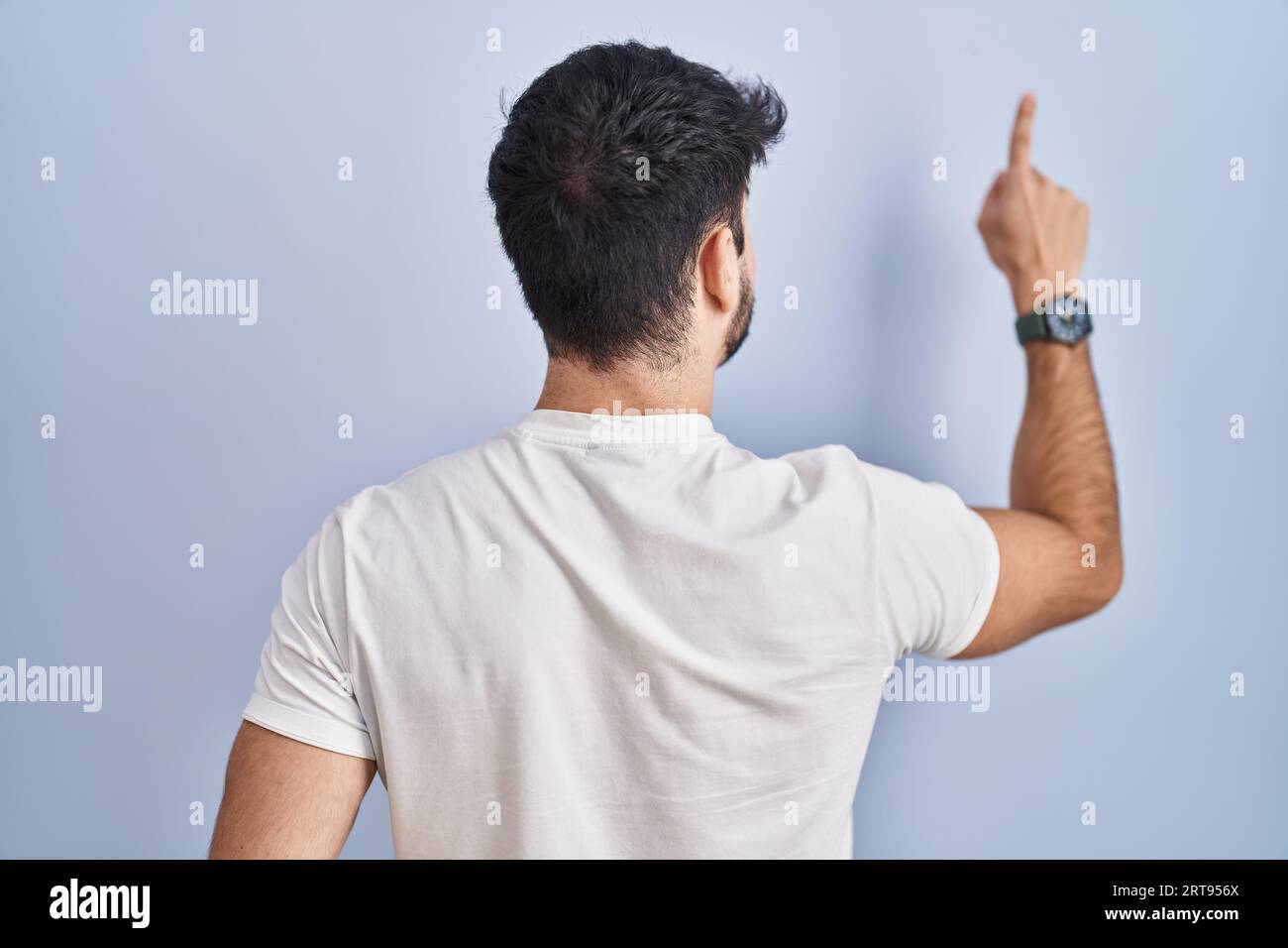 Hispanic man with beard standing over white background posing backwards ...