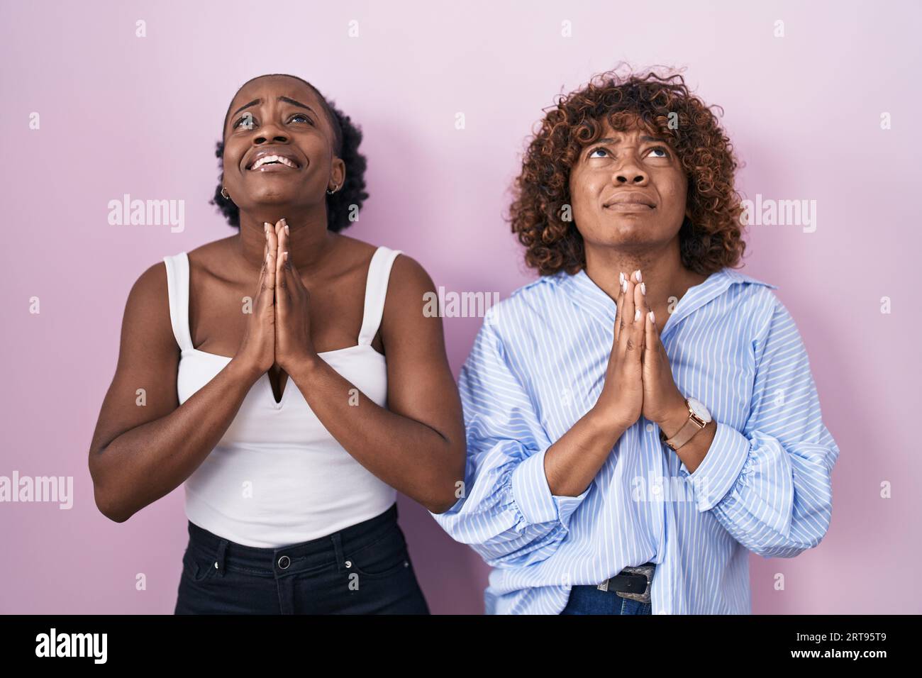 Two african women standing over pink background begging and praying ...