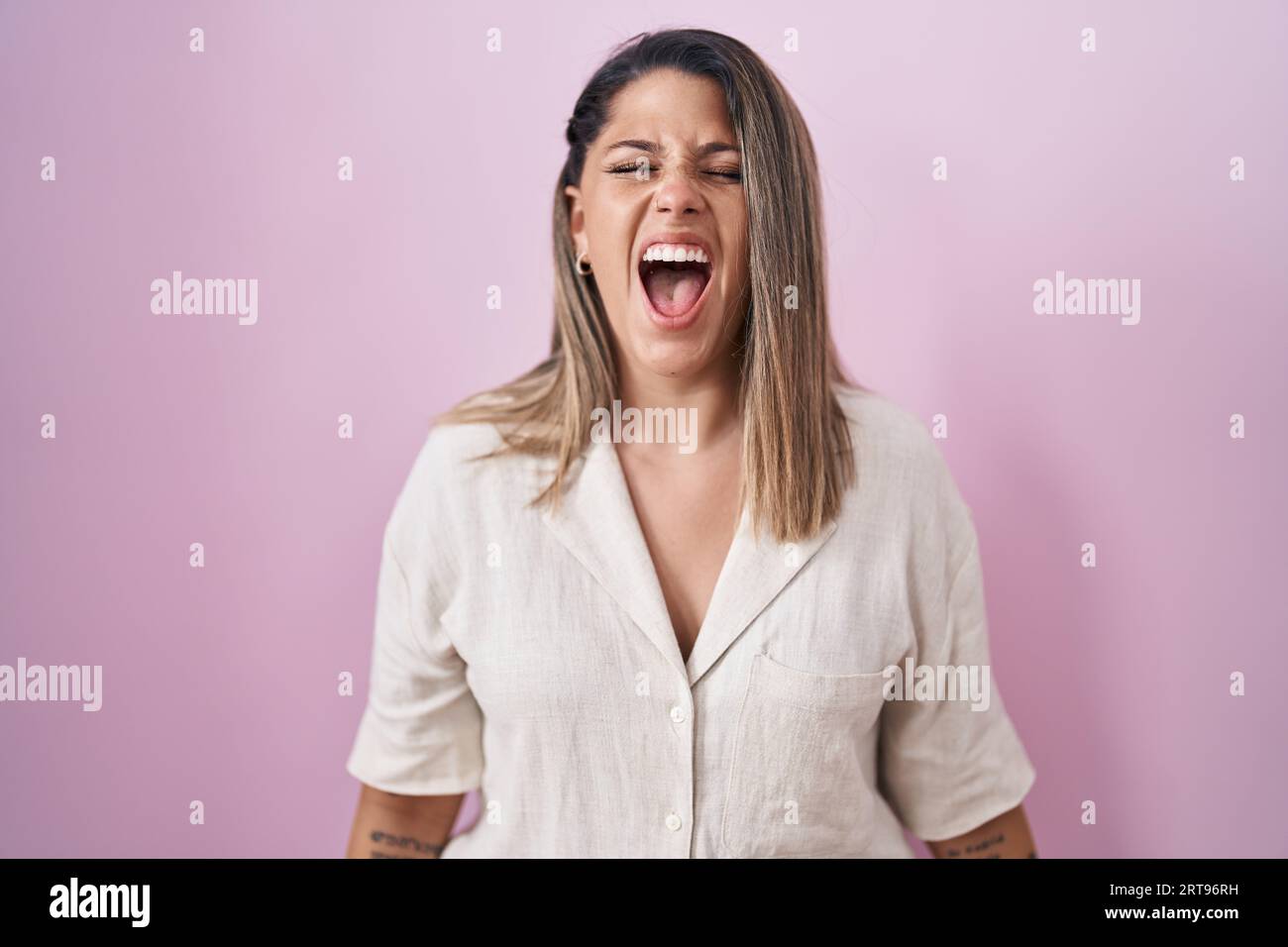 Blonde woman standing over pink background angry and mad screaming ...