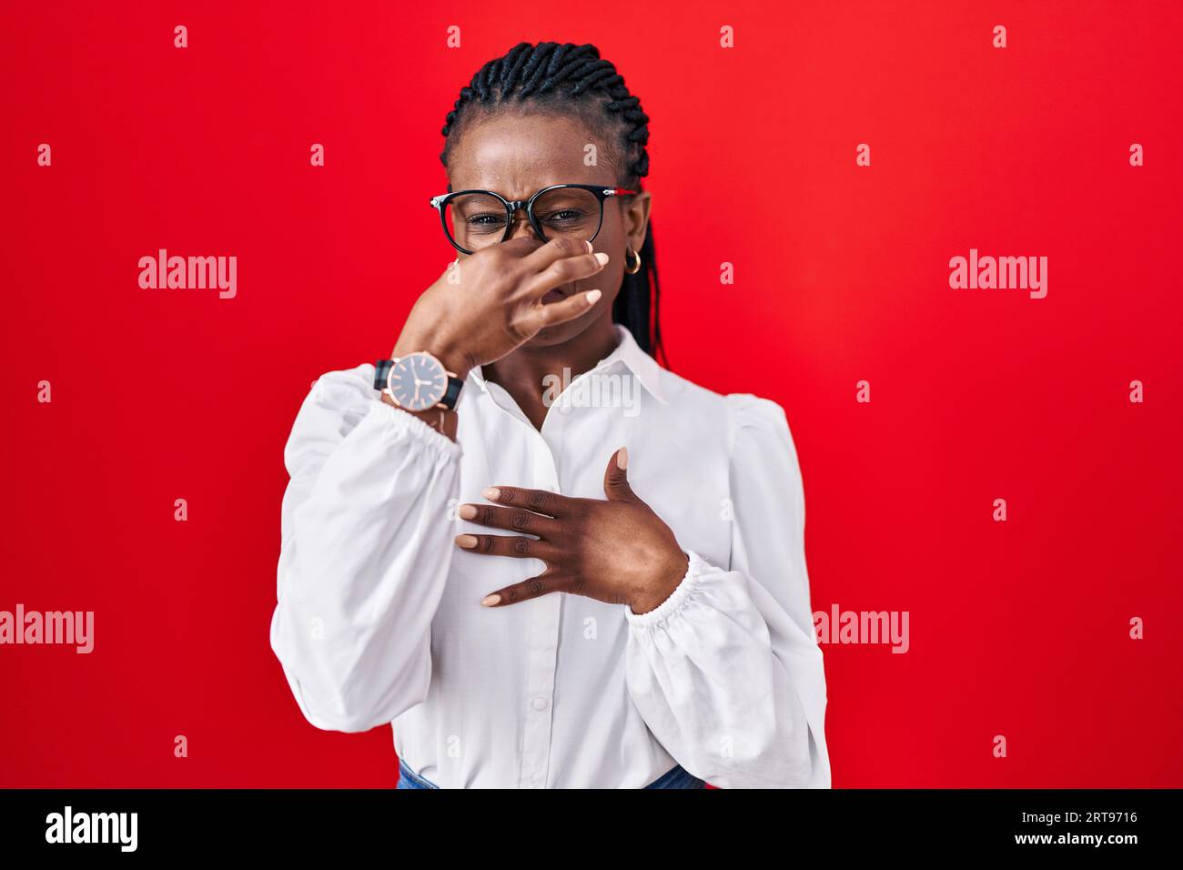 African woman with braids standing over red background smelling ...