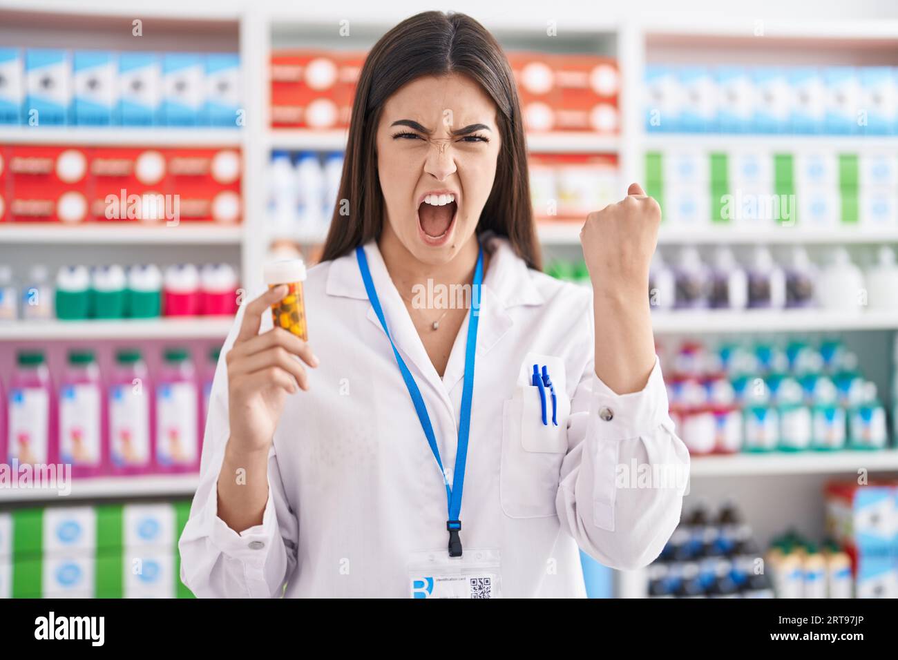 Hispanic woman working at pharmacy drugstore holding pills annoyed and ...