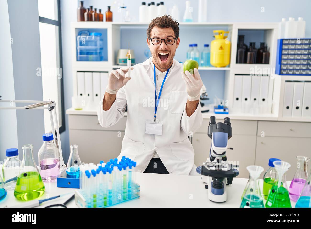 Young hispanic man working at scientist laboratory holding apple ...