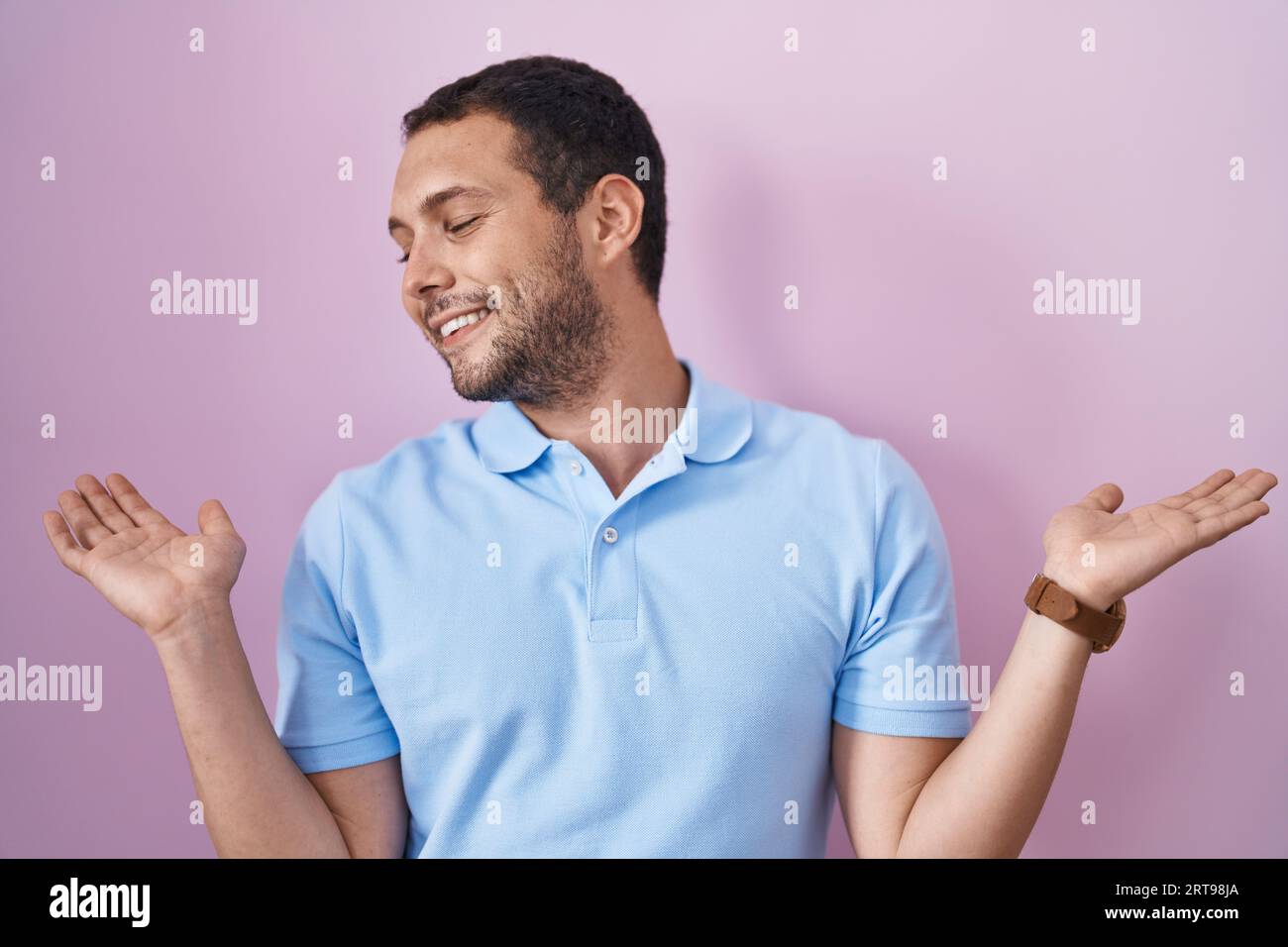 Hispanic man standing over pink background smiling showing both hands ...