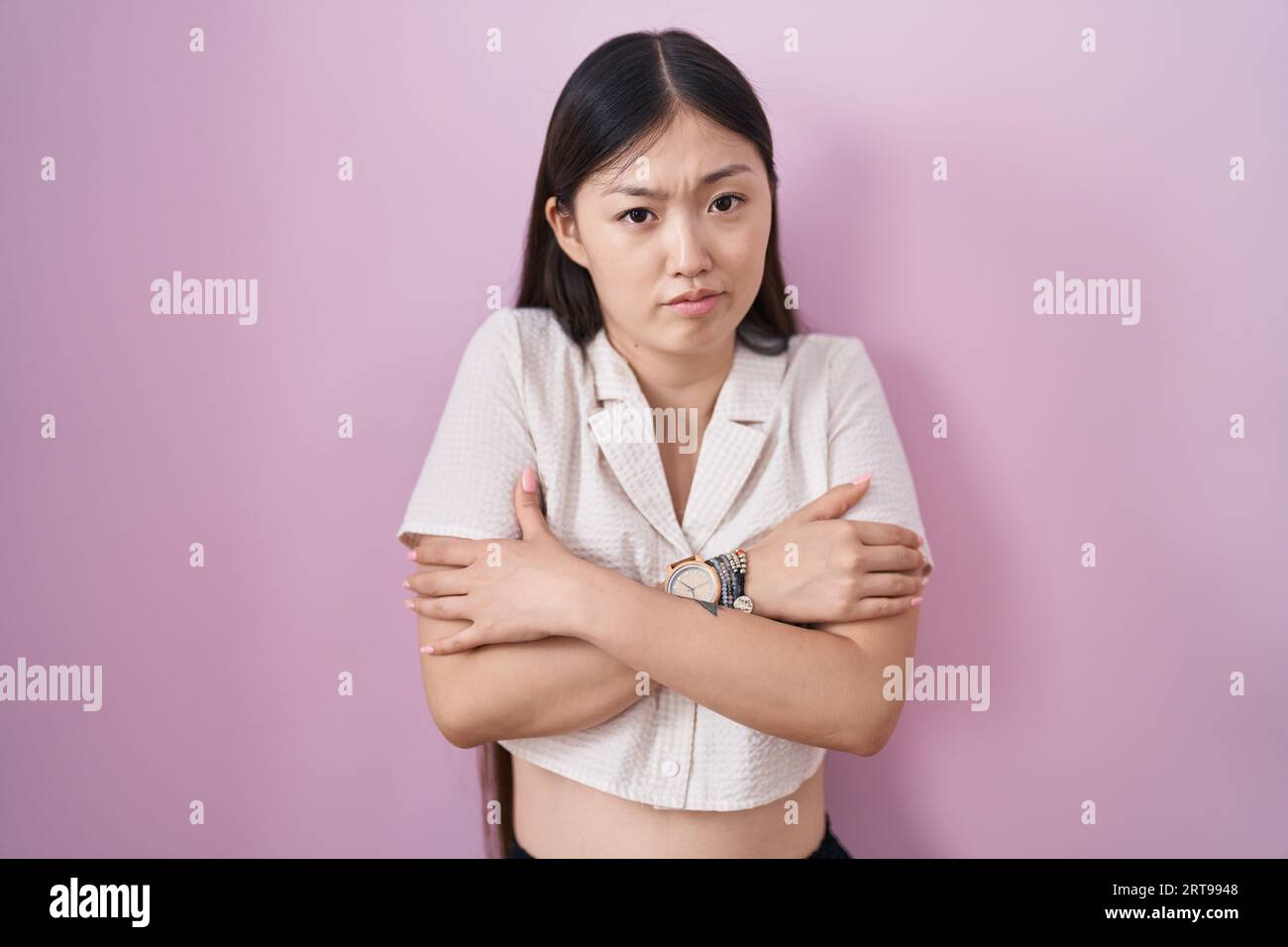 Chinese young woman standing over pink background shaking and freezing ...