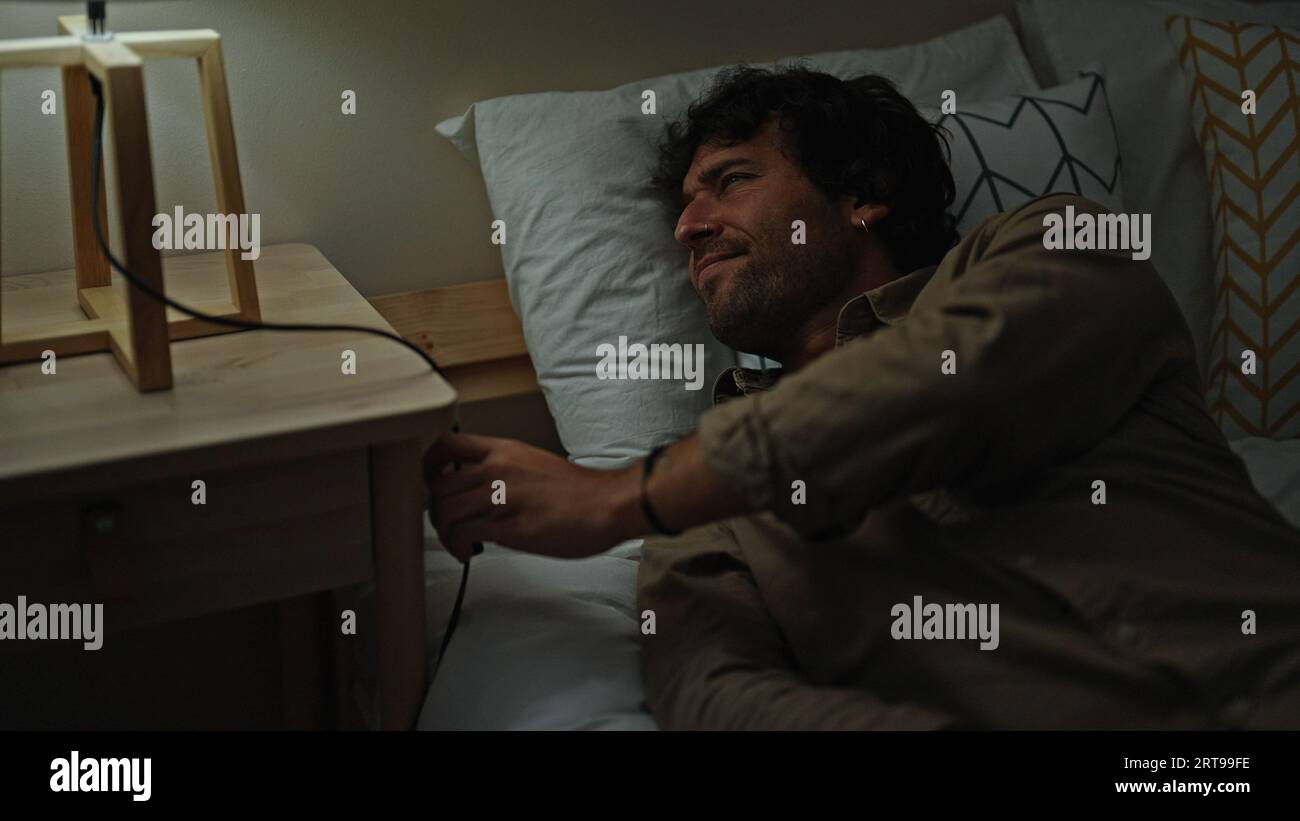 Young hispanic man lying on bed tired turning light off to sleep at ...
