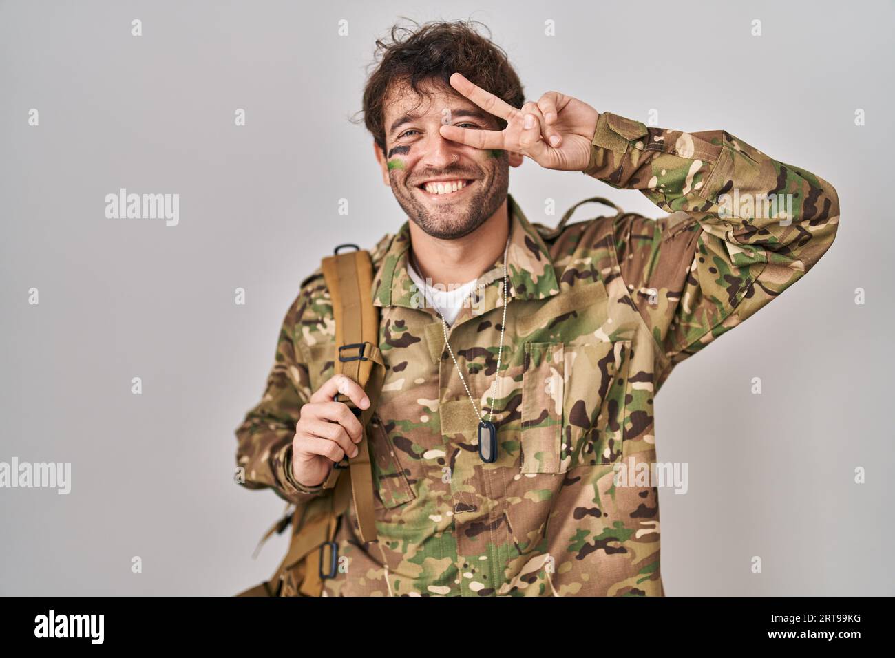 Hispanic young man wearing camouflage army uniform doing peace symbol ...