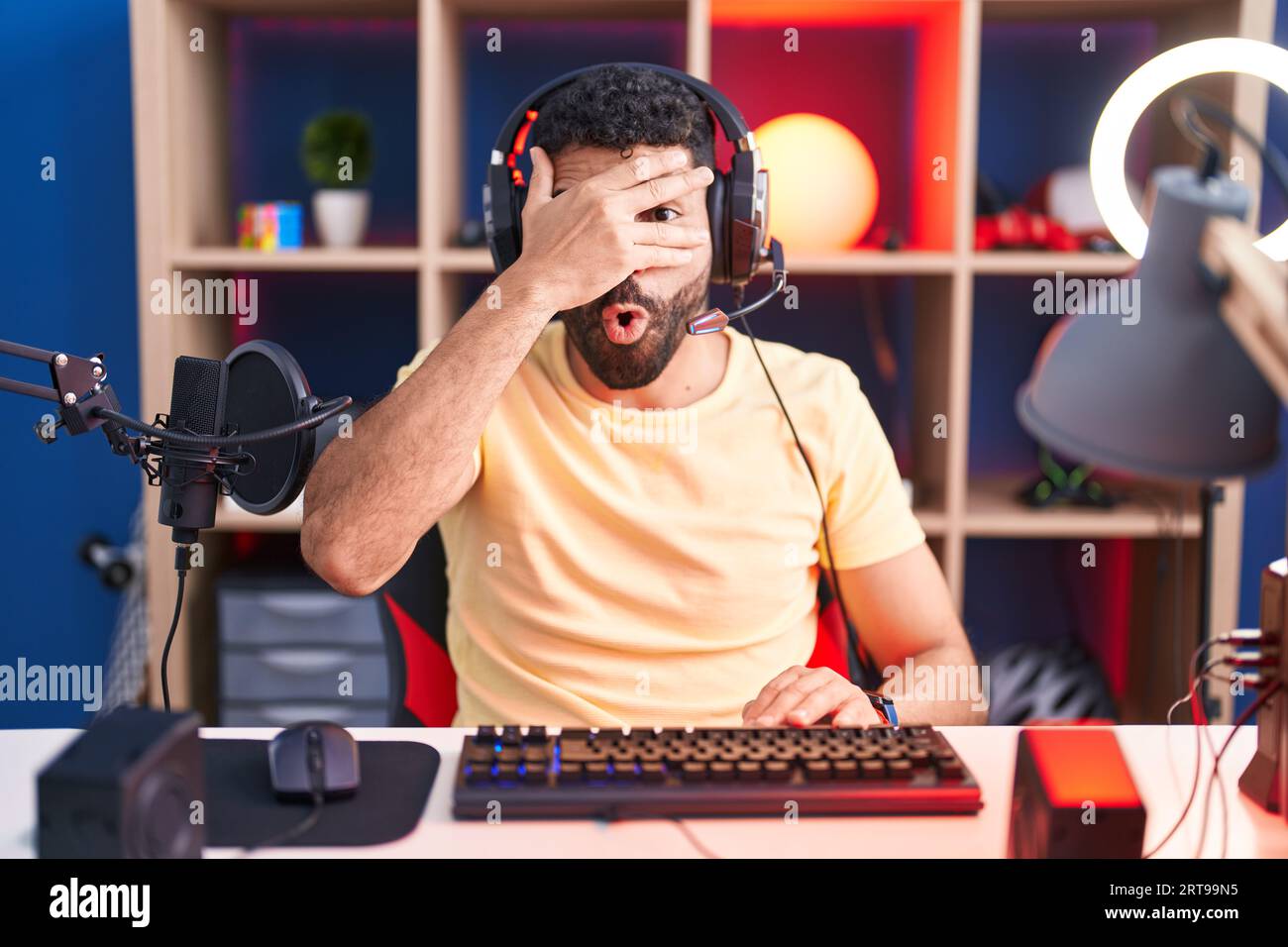 Hispanic man with beard playing video games with headphones peeking in ...