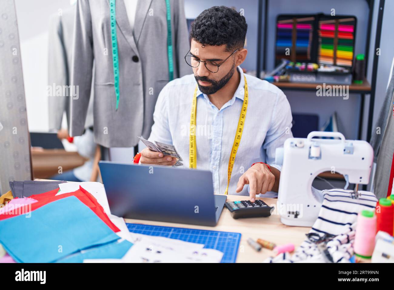 Young arab man tailor using laptop counting dollars at tailor shop ...