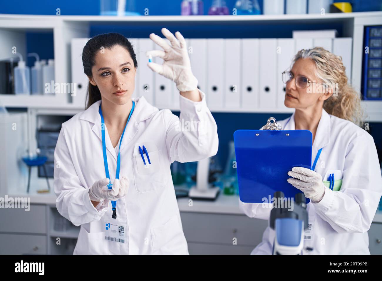 Two women scientists holding pills write on document at laboratory ...