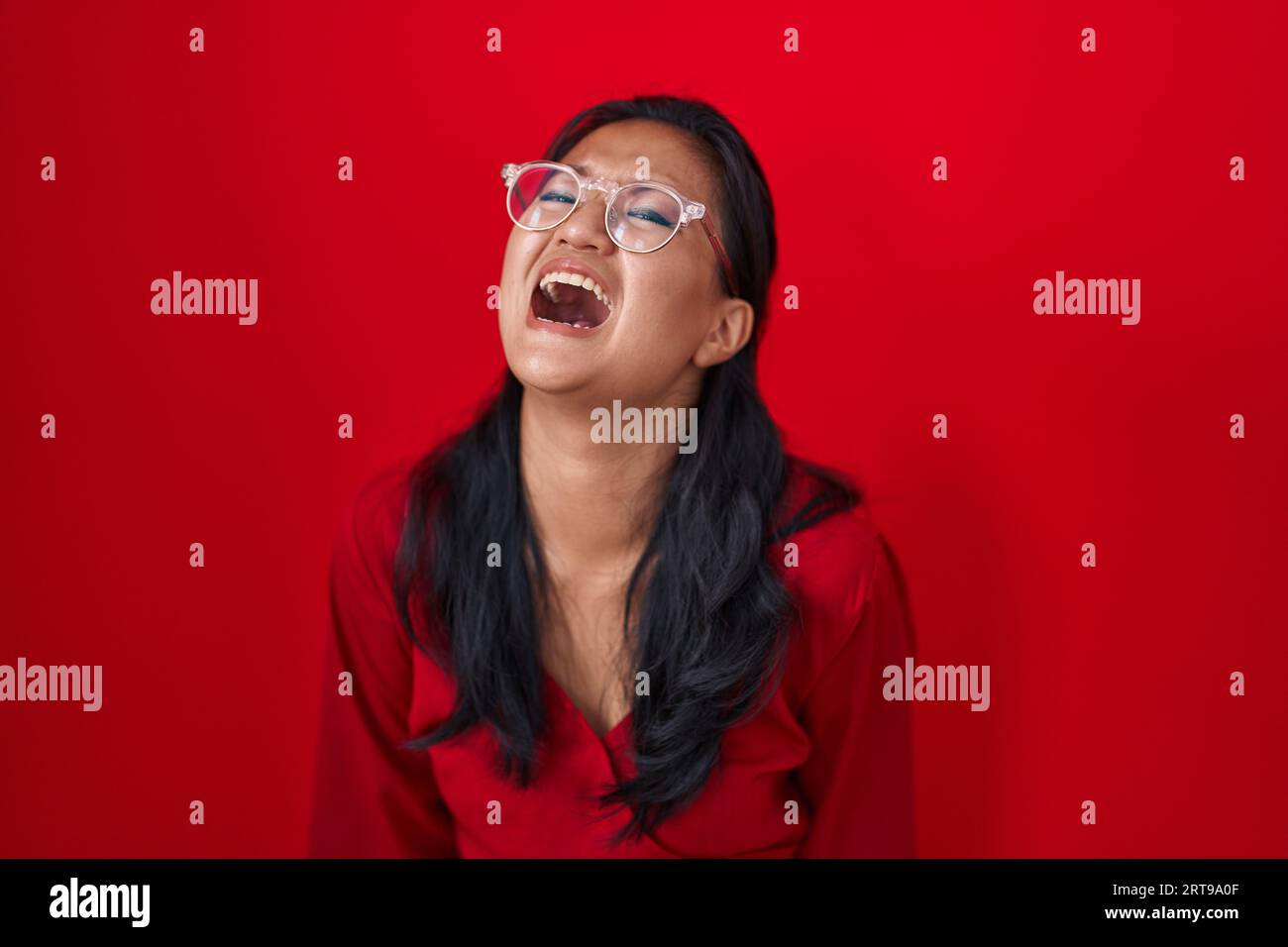 Asian young woman standing over red background angry and mad screaming ...