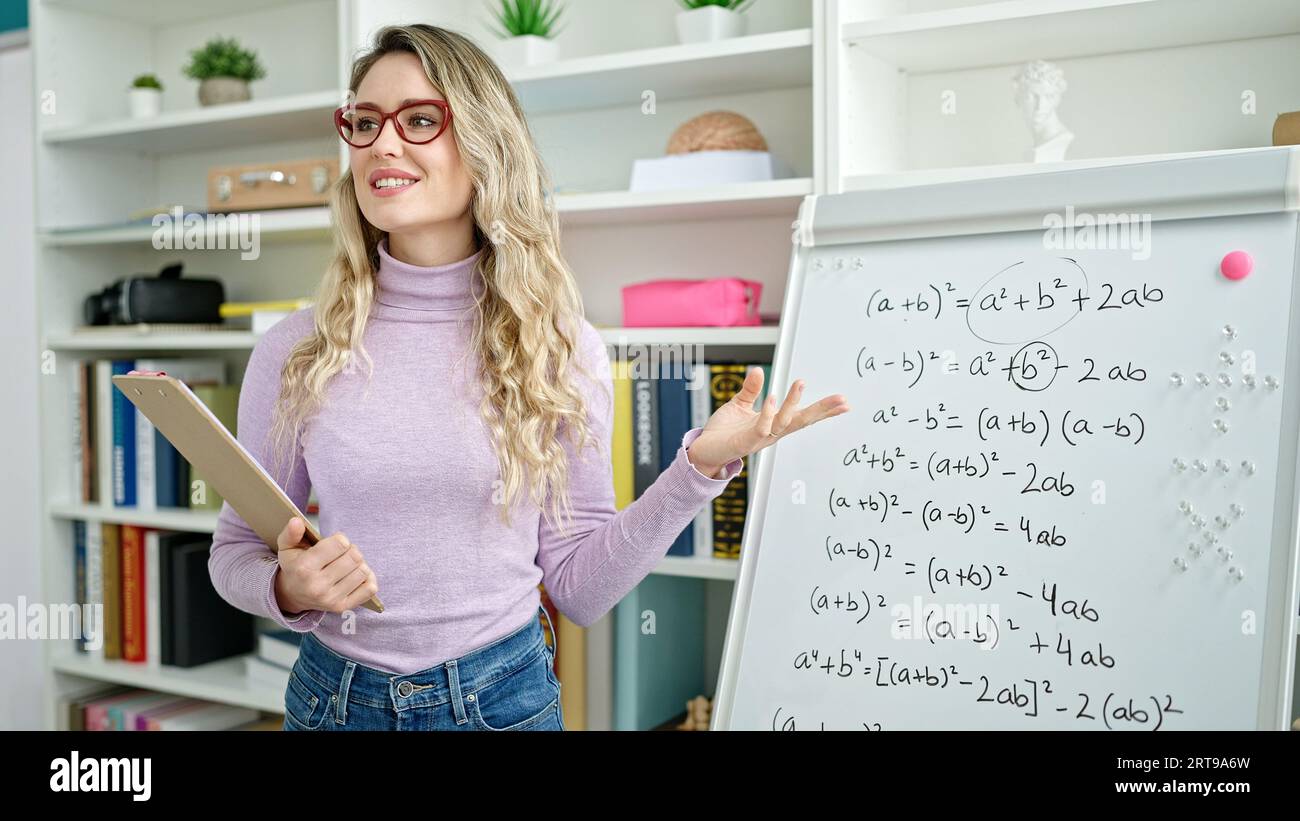Young blonde woman teacher teaching maths lesson holding clipboard at ...