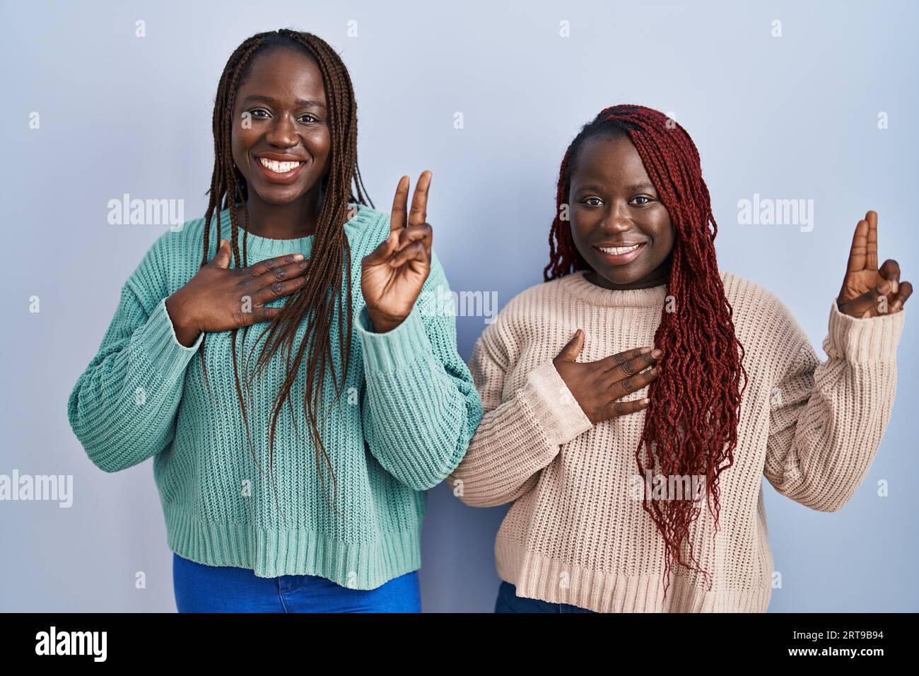 Two african woman standing over blue background smiling swearing with ...