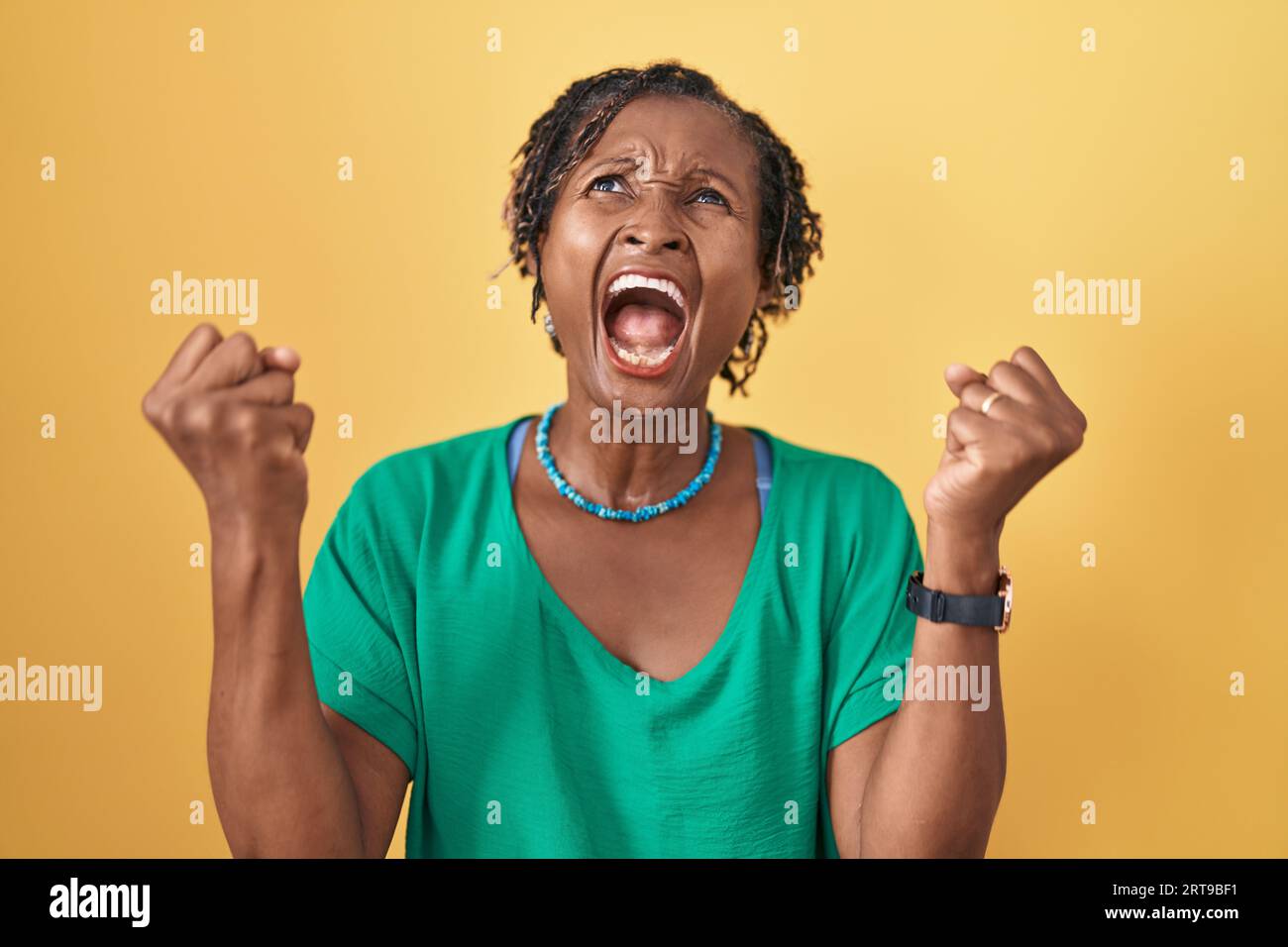 African woman with dreadlocks standing over yellow background angry and ...