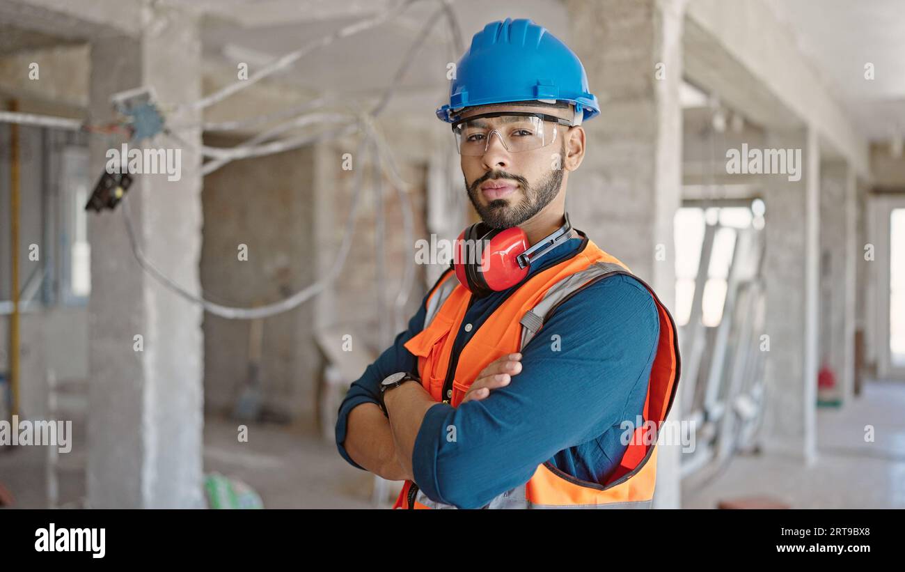 Young hispanic man builder with crossed arms wearing hardhat at ...