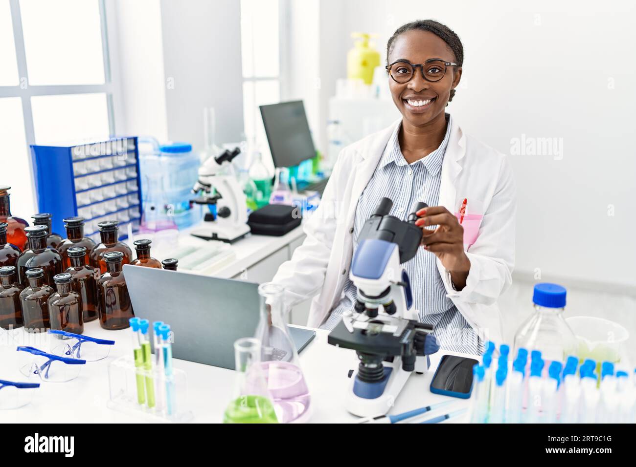African american woman scientist using laptop and microscope at ...