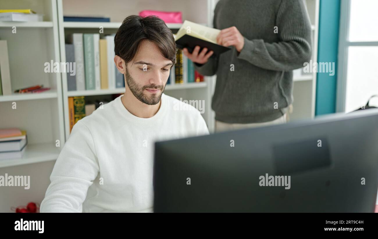 Two men students using computer reading book studying at library university Stock Photo - Alamy