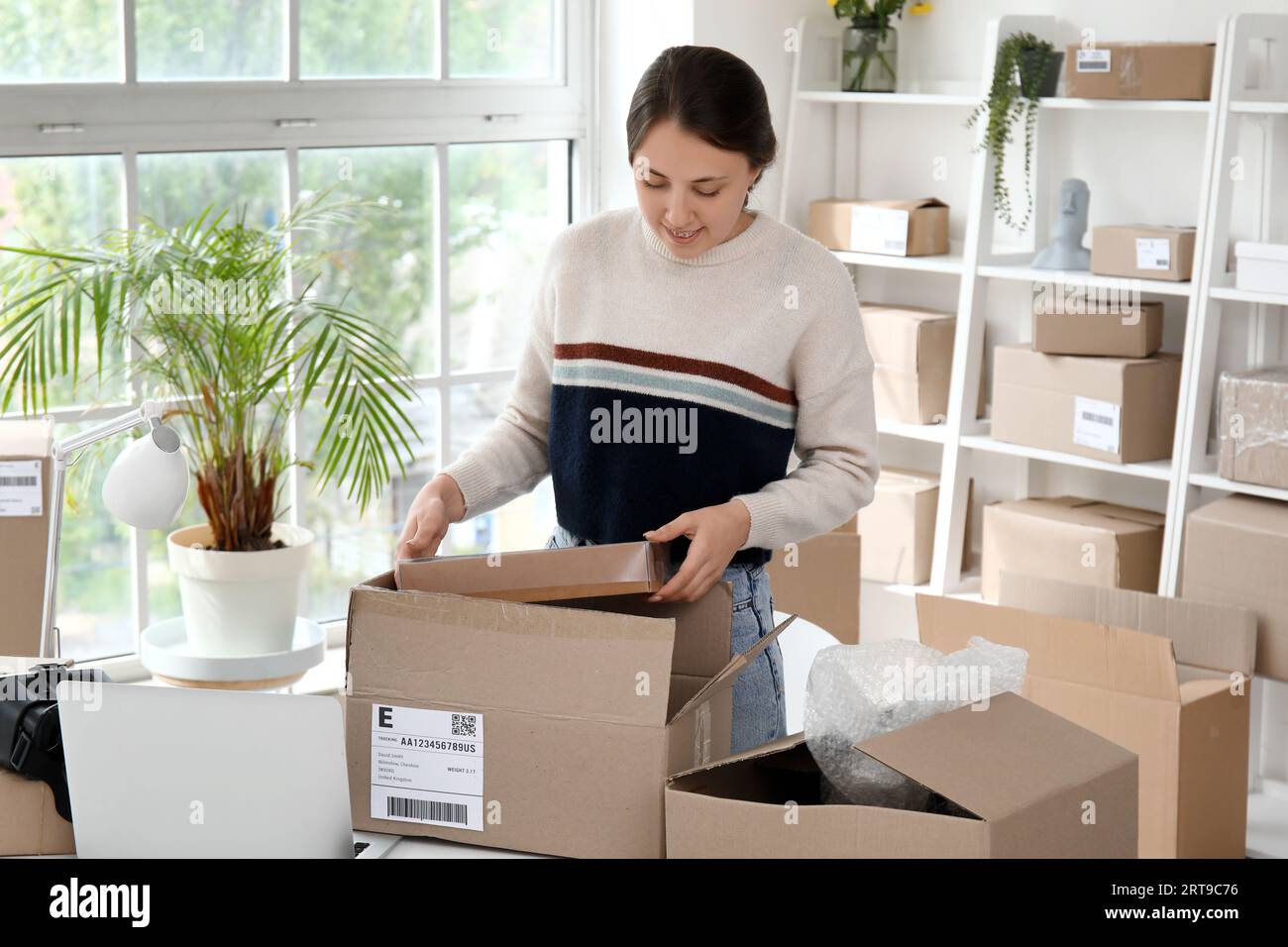 Young woman packing parcel for client in office Stock Photo - Alamy