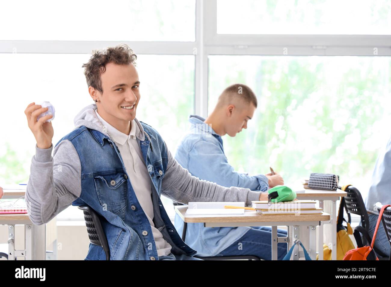 Male student throwing crumpled paper in his classmates at classroom ...