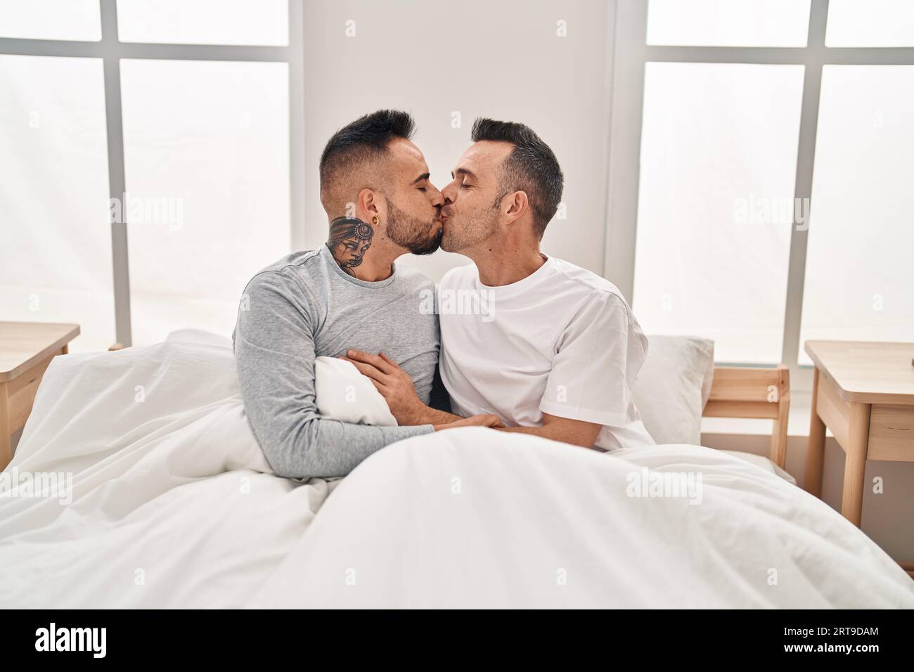 Two men couple sitting on bed hugging each other kissing at bedroom Stock Photo - Alamy