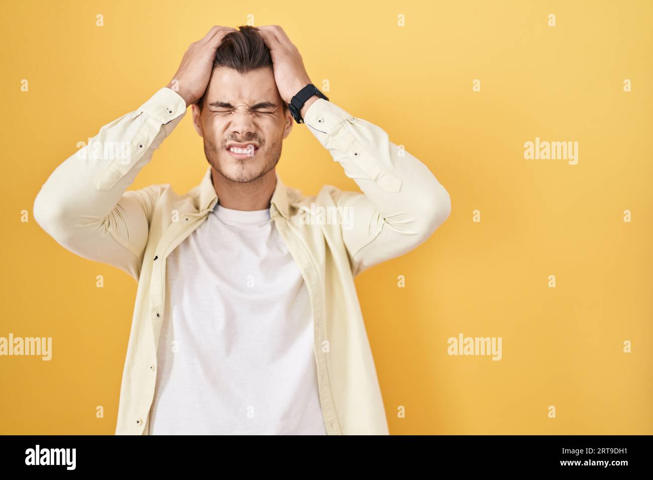 Young hispanic man standing over yellow background suffering from ...