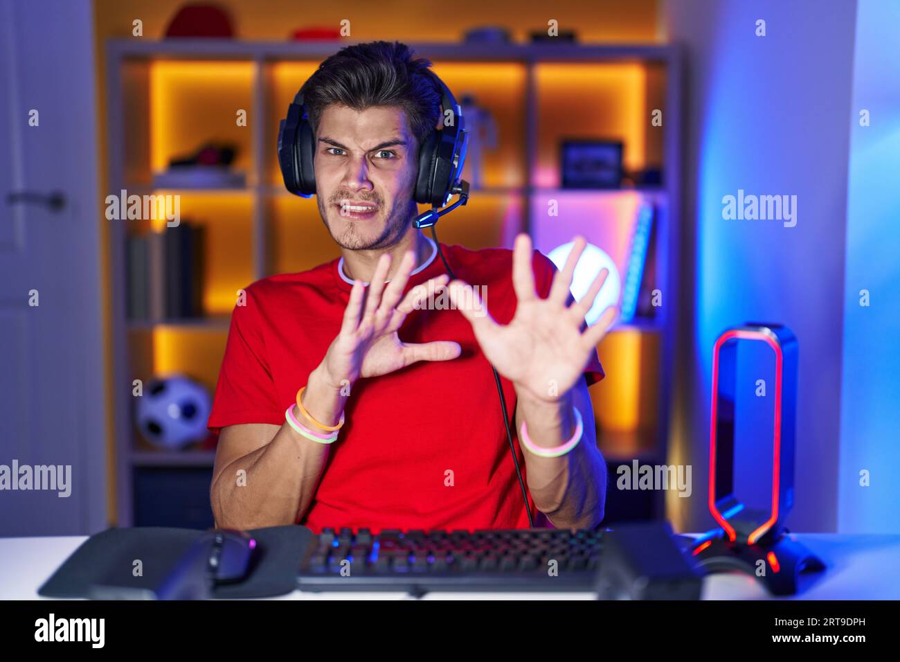 Young hispanic man playing video games disgusted expression, displeased ...