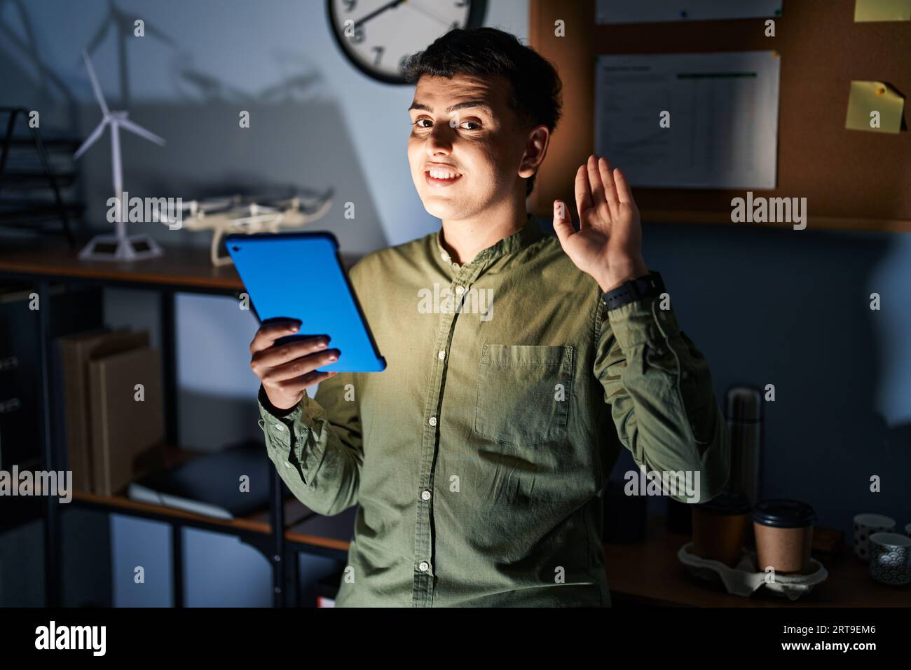 Non binary person using touchpad device at night waiving saying hello happy and smiling ...