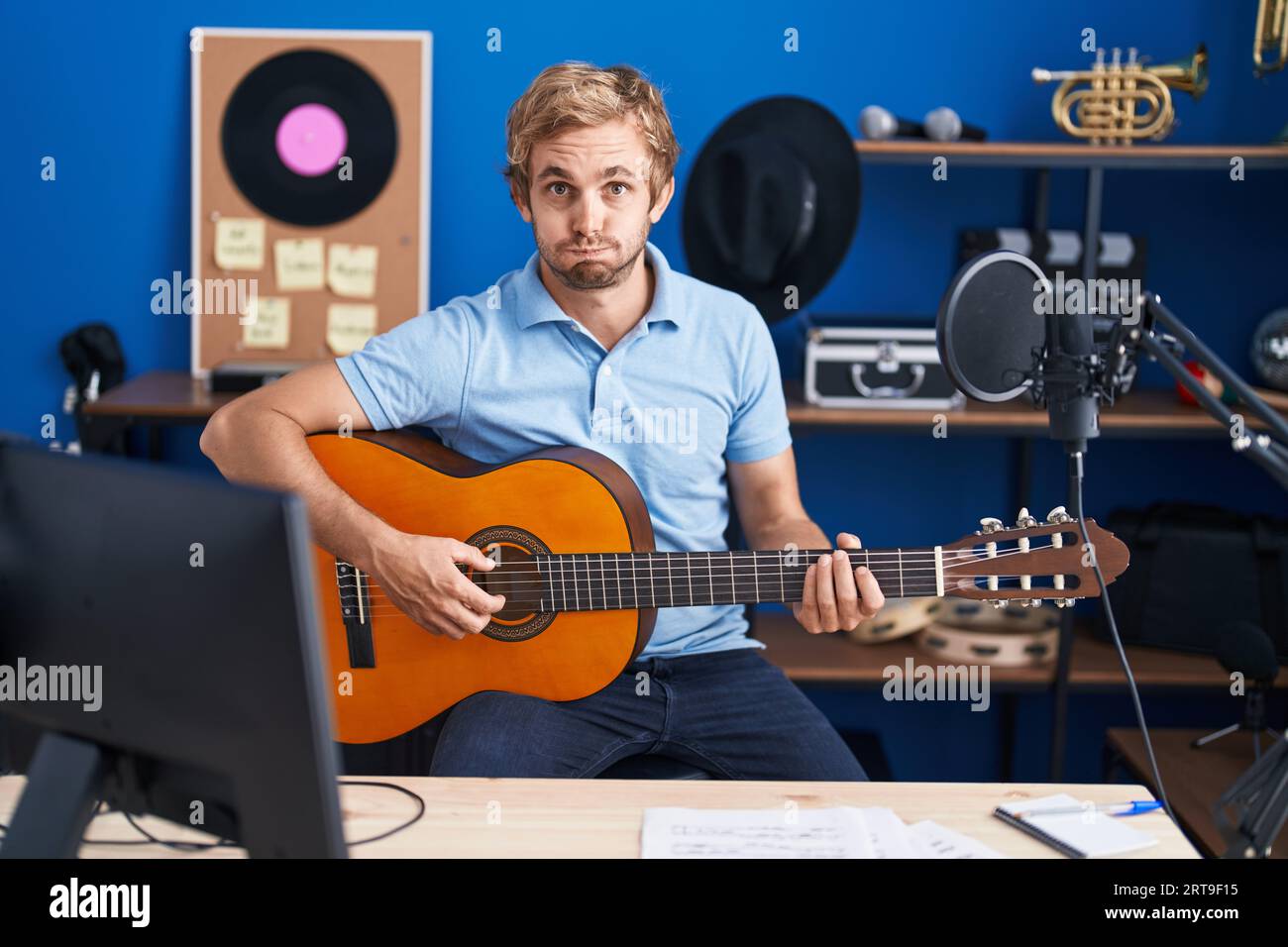 Caucasian man playing classic guitar at music studio puffing cheeks ...