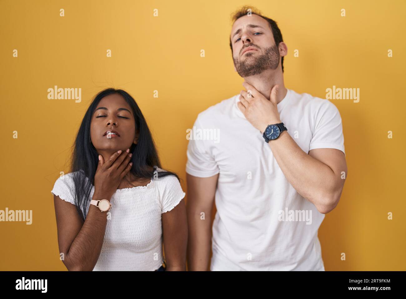 Interracial couple standing over yellow background touching painful ...
