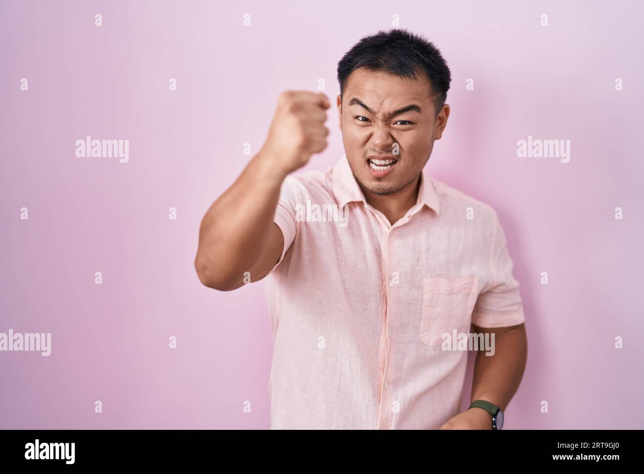 Chinese young man standing over pink background angry and mad raising ...