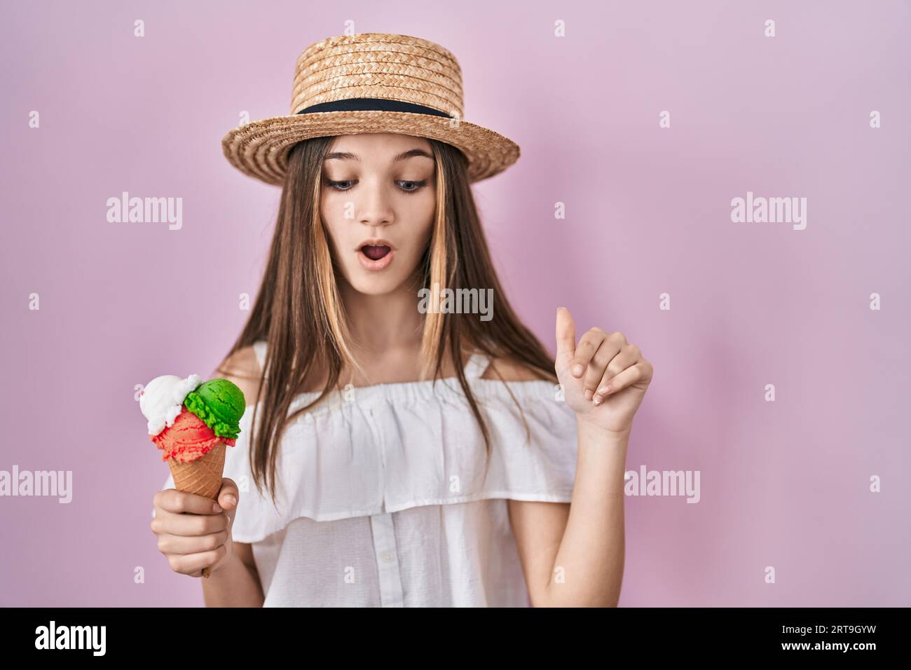 Teenager girl holding ice cream pointing down with fingers showing ...