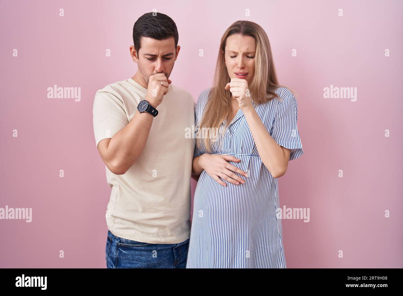 Young couple expecting a baby standing over pink background feeling ...