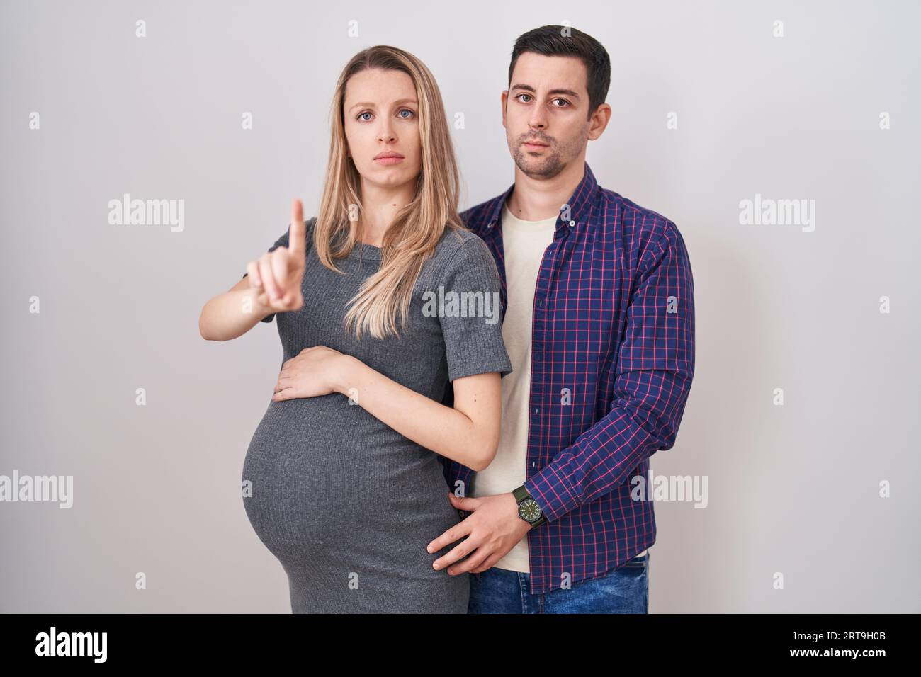 Young couple expecting a baby standing over white background pointing ...