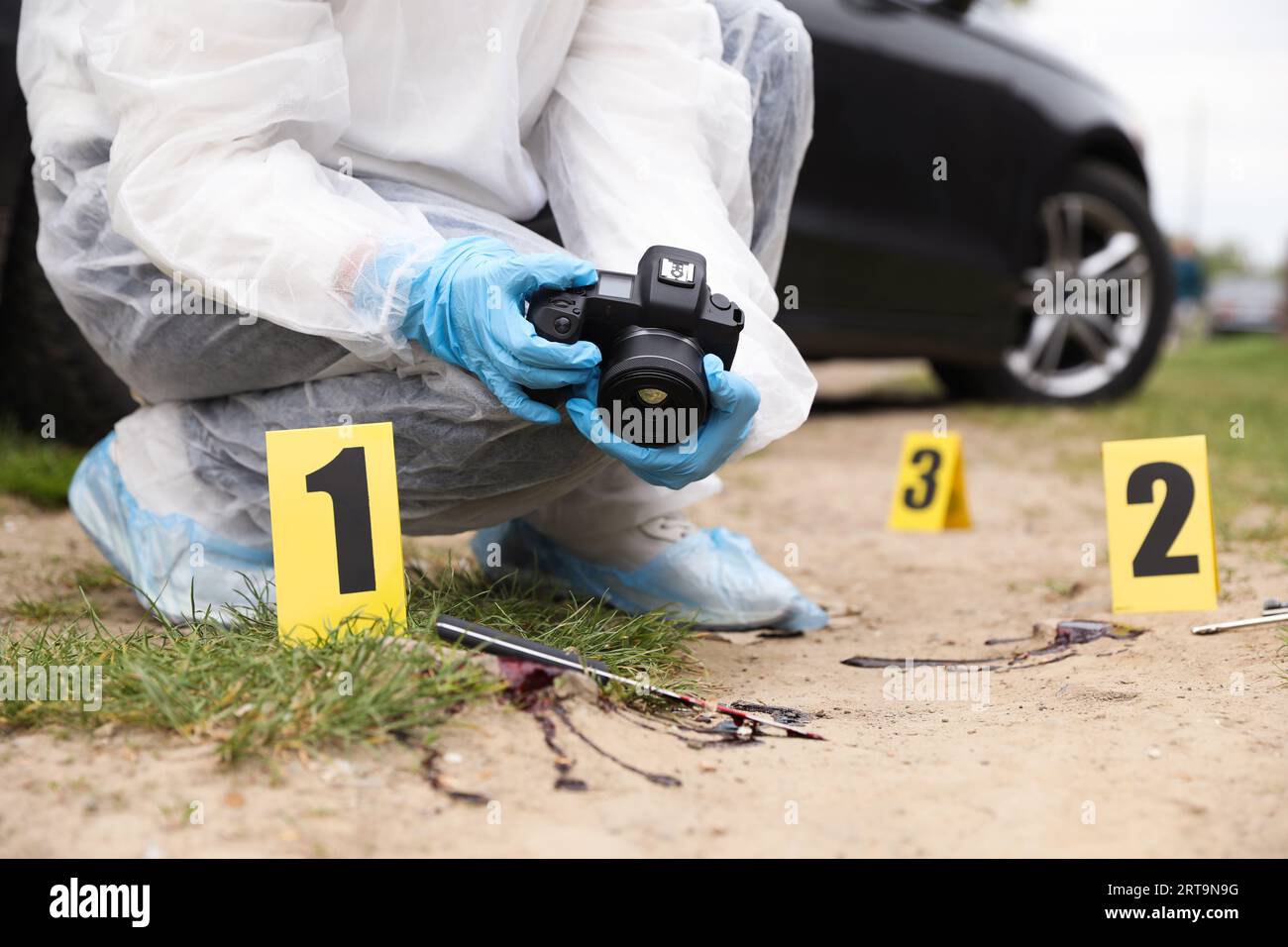 Criminologist in protective suit taking photo of evidence at crime scene outdoors, closeup Stock ...