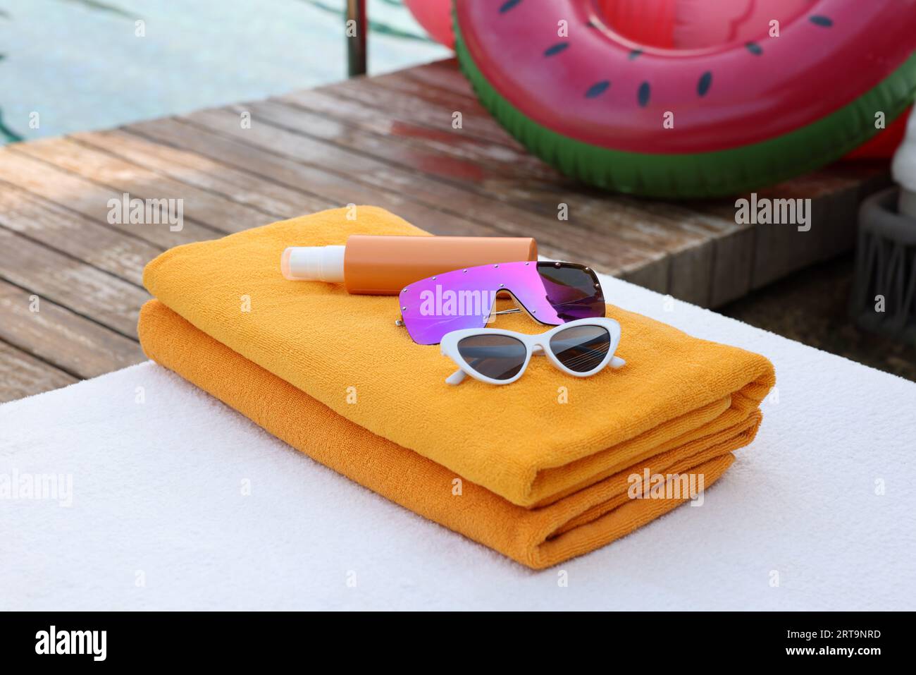 Beach towels, sunglasses and sunscreen on sunbed near outdoor swimming ...