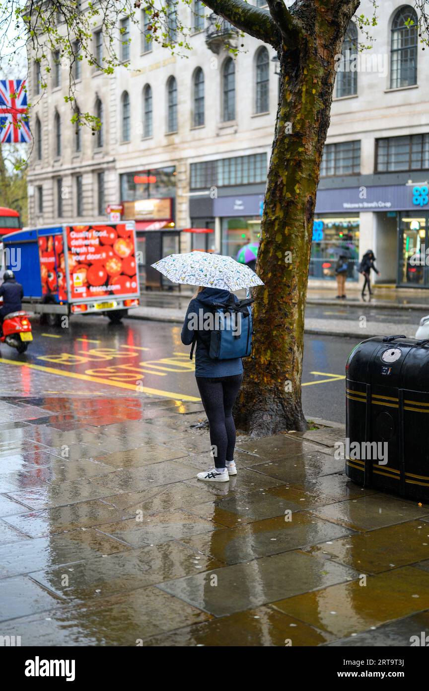 LONDON - April 24, 2023: A woman with an umbrella and a backpack ...