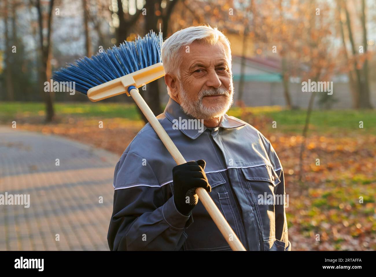 Smiling maintenance male worker looking at camera, while keeping broom ...