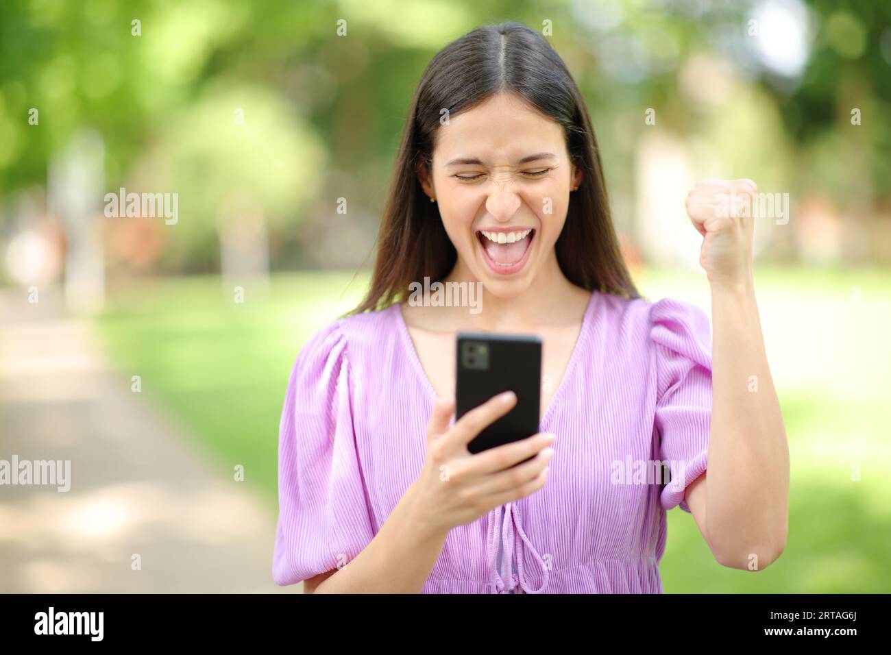Front view portrait of an excited woman checking cell phone content outdoor Stock Photo - Alamy