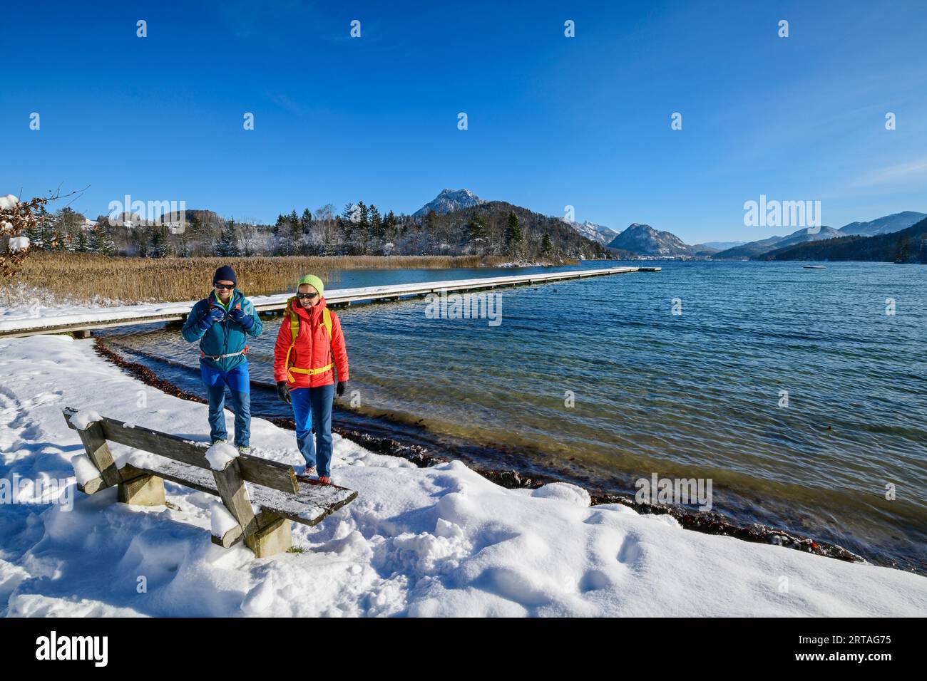 Man and woman hiking walking towards bench on the shore of Lake Fuschl ...