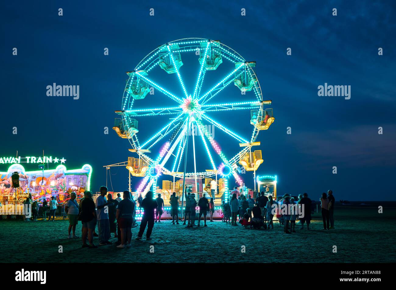 Funfair at night on beach in summer. Runaway Train and Ferris wheel ...