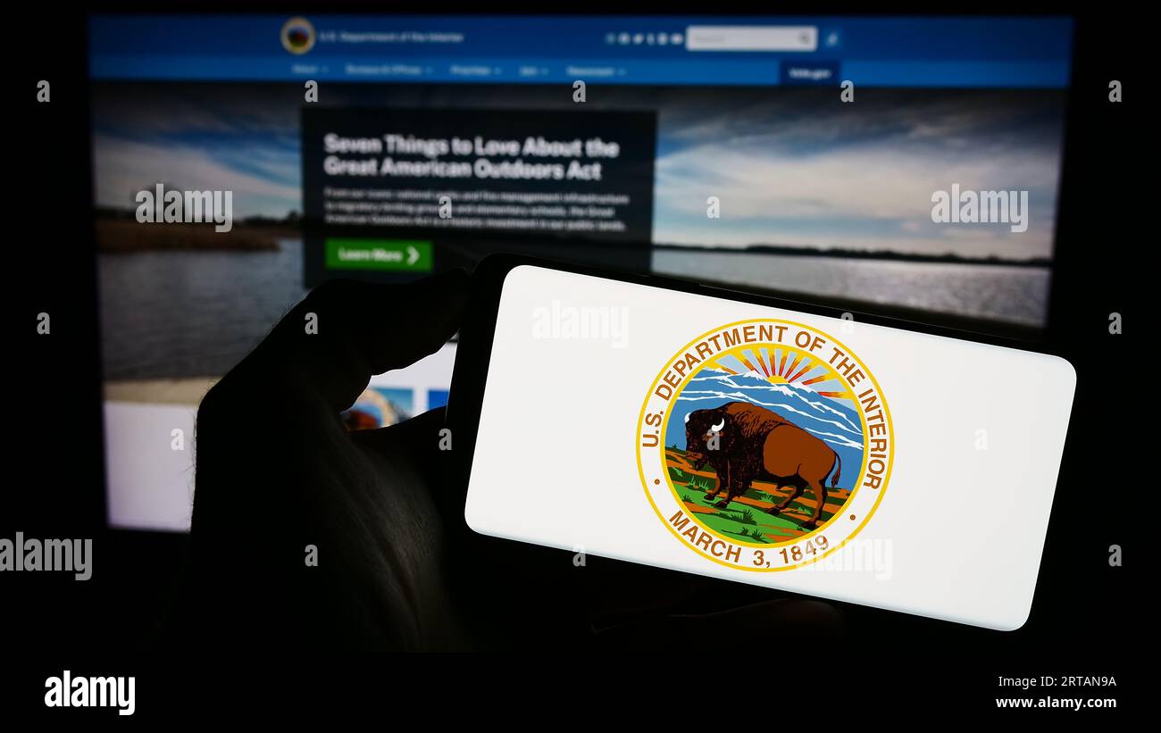 Person holding mobile phone with seal of United States Department of ...