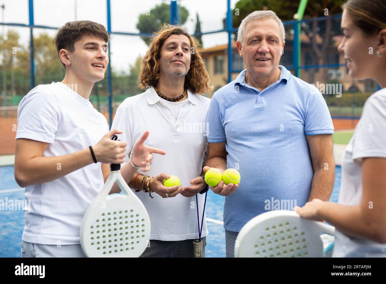 Four positive tennis players of different ages discussing preparing for ...