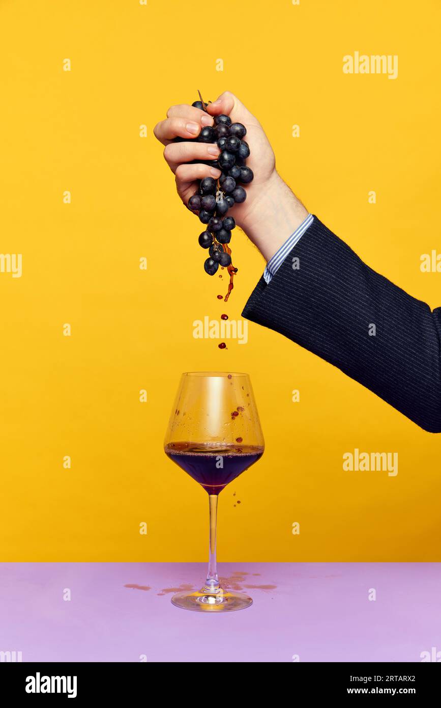 Male hand squeezing grape juice into wine glass over bright yellow ...
