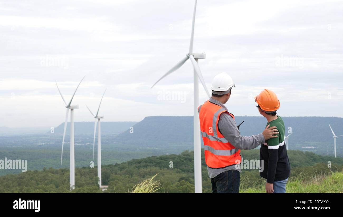Engineer with his son on a wind farm atop a hill or mountain in the ...