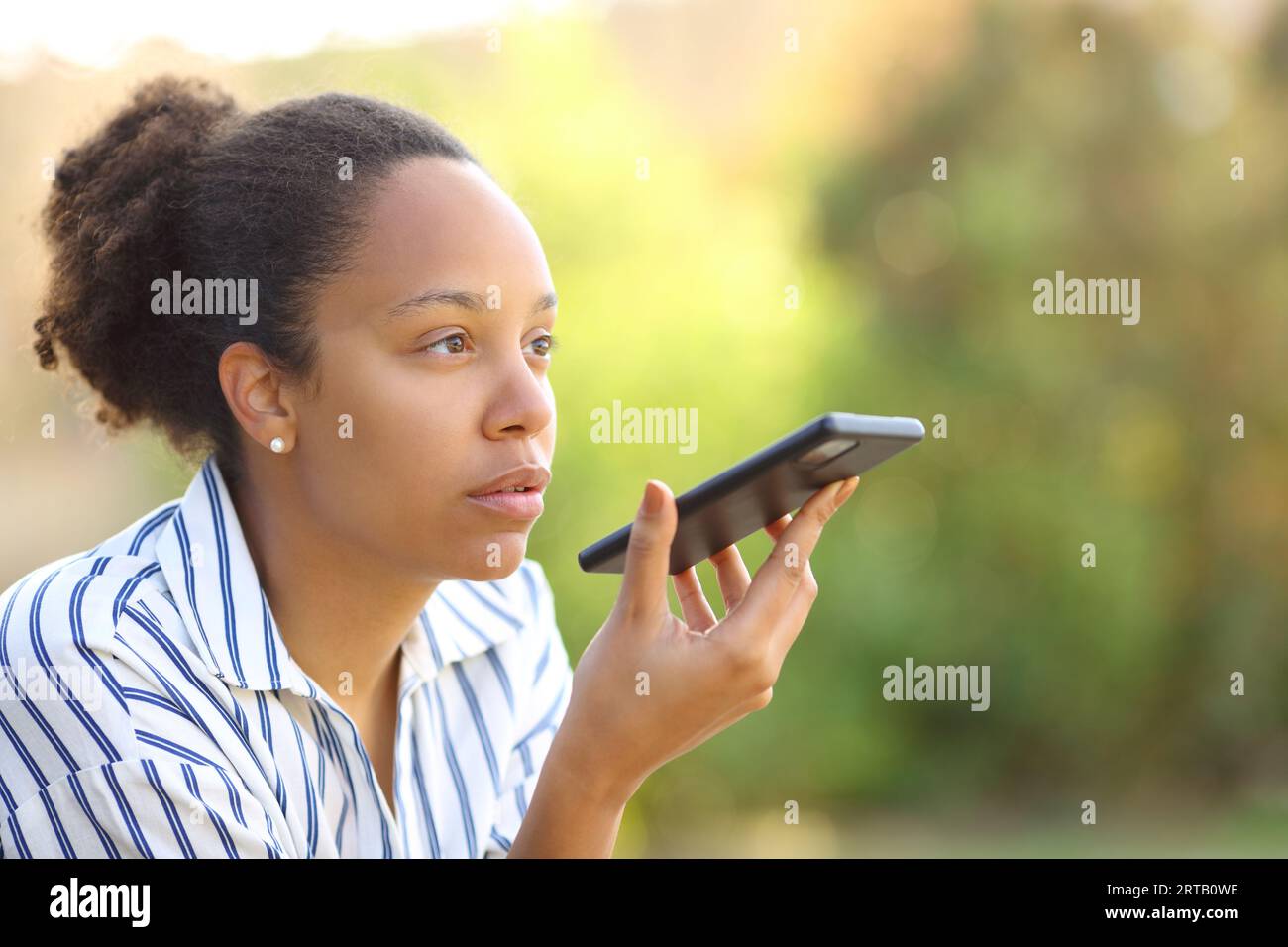 Black woman dictating text on phone usig voice recognition siting in a ...