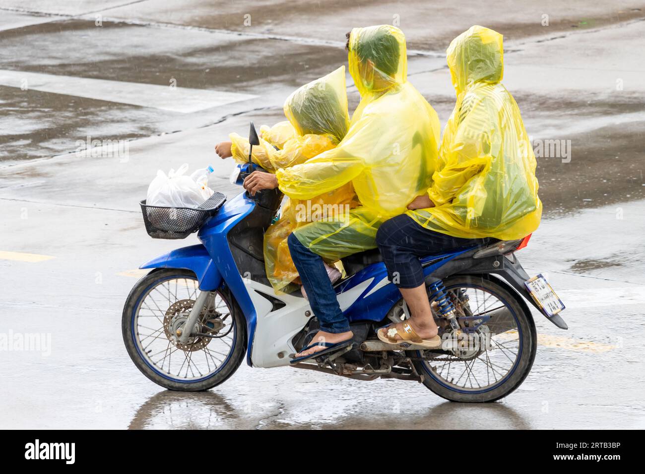 A family dressed in raincoats is riding a motorcycle in the rain ...