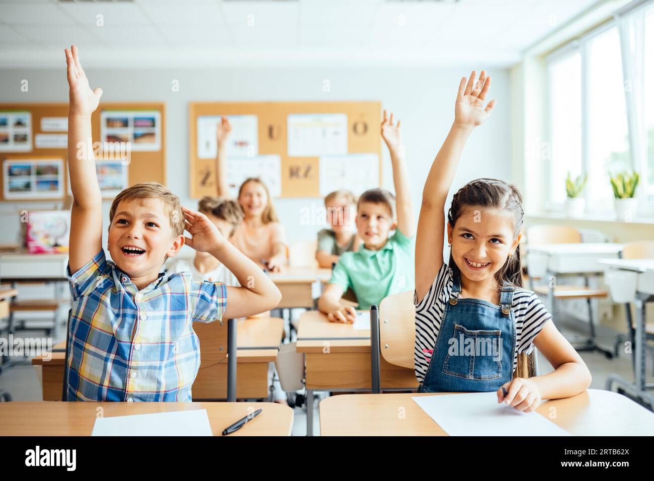 School children in classroom at lesson. Little children raising hands ...