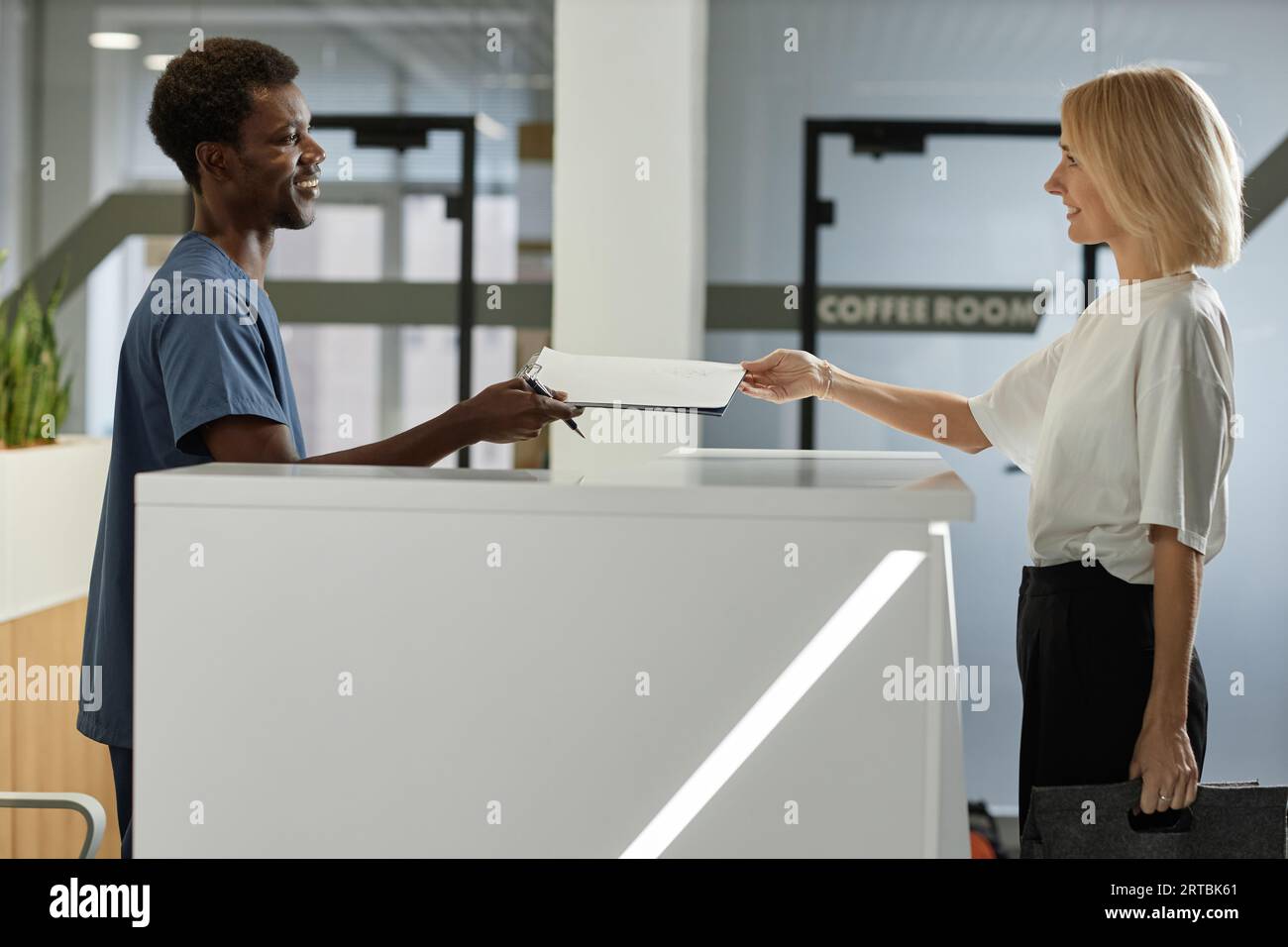 Side view of young female patient of clinics passing document to male ...